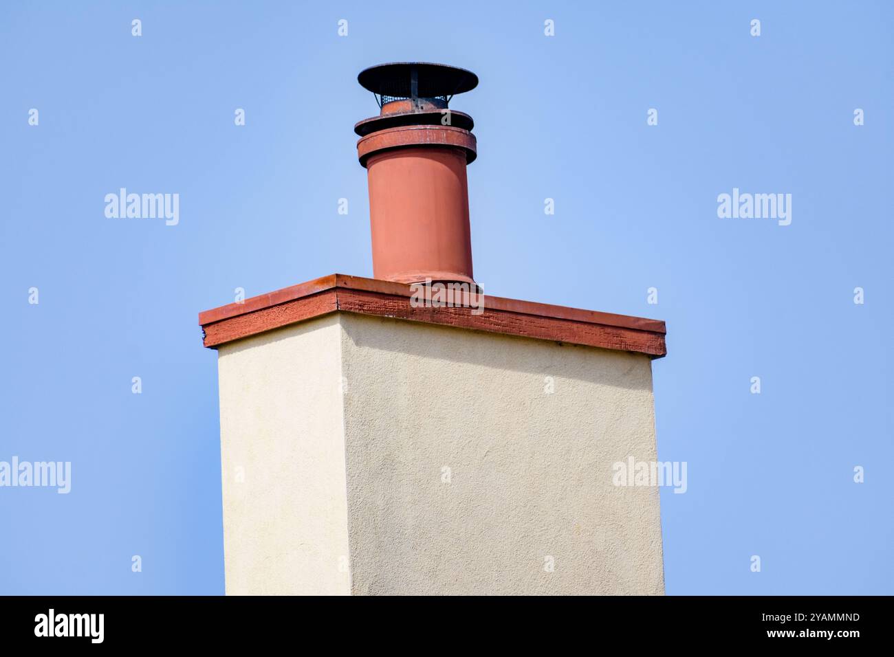 A red metal chimney cap sits atop a beige stucco chimney against a ...