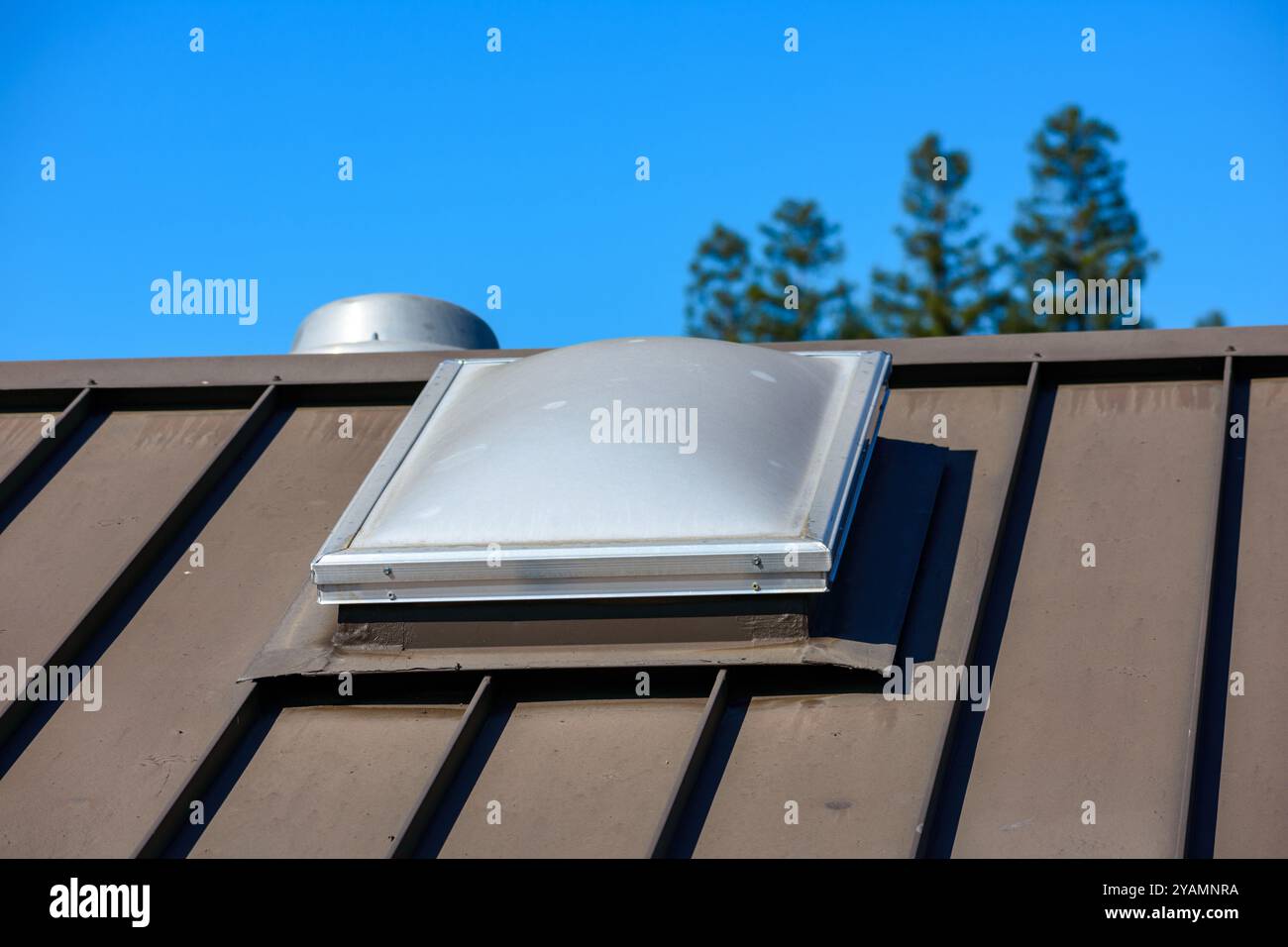 A sleek rectangular skylight on a brown metal roof, with a clear blue ...