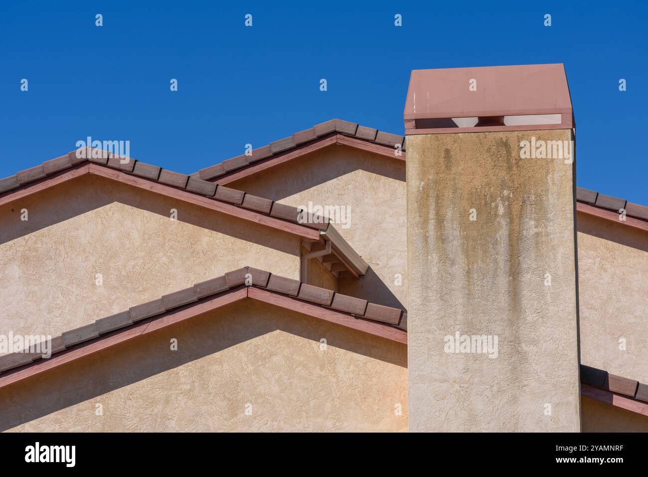 A tall stucco chimney shows discoloration and weathering, rising beside ...