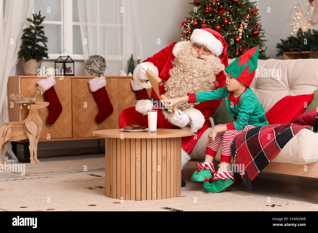 Santa Claus and cute little elf reading letter at home on Christmas eve ...