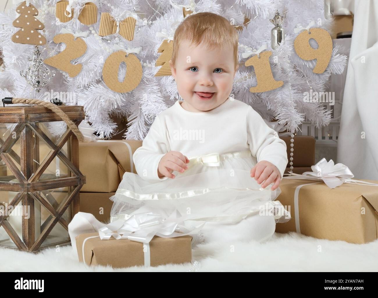 Lovely little girl (eight months of age) in a white dress sitting under ...