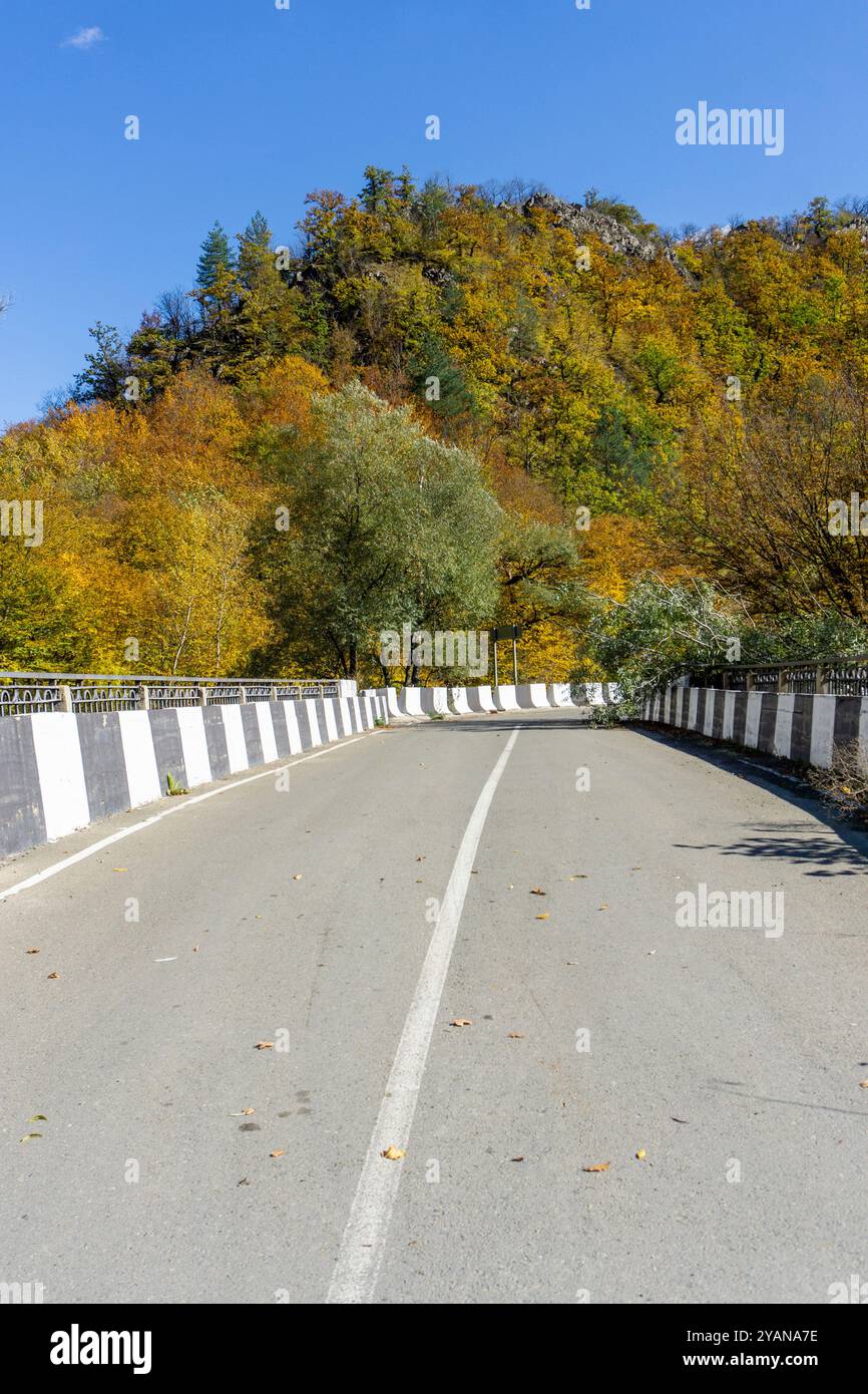 An asphalt road with markings and high curbs leads to a hill with ...