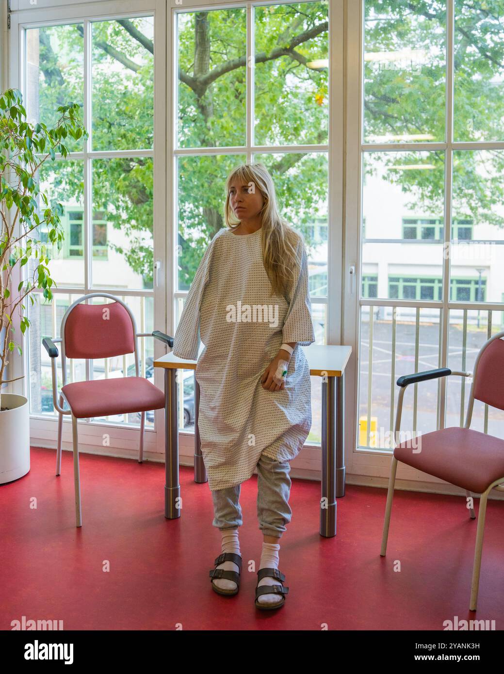 Injured woman standing against window in hospital with an intravenous ...