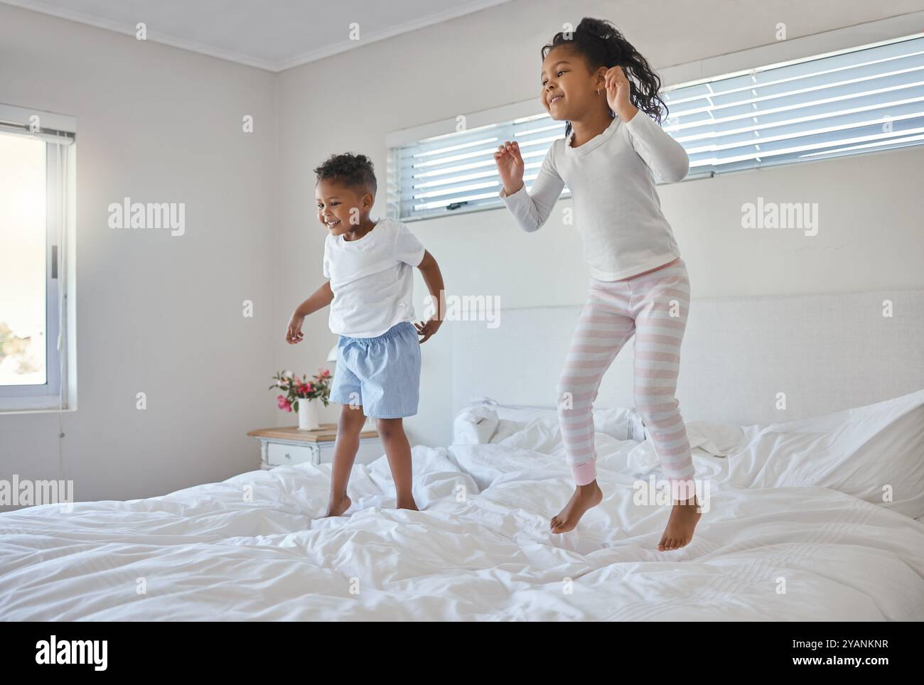 Happy kids, morning and jump on bed in home for playing, bonding or ...