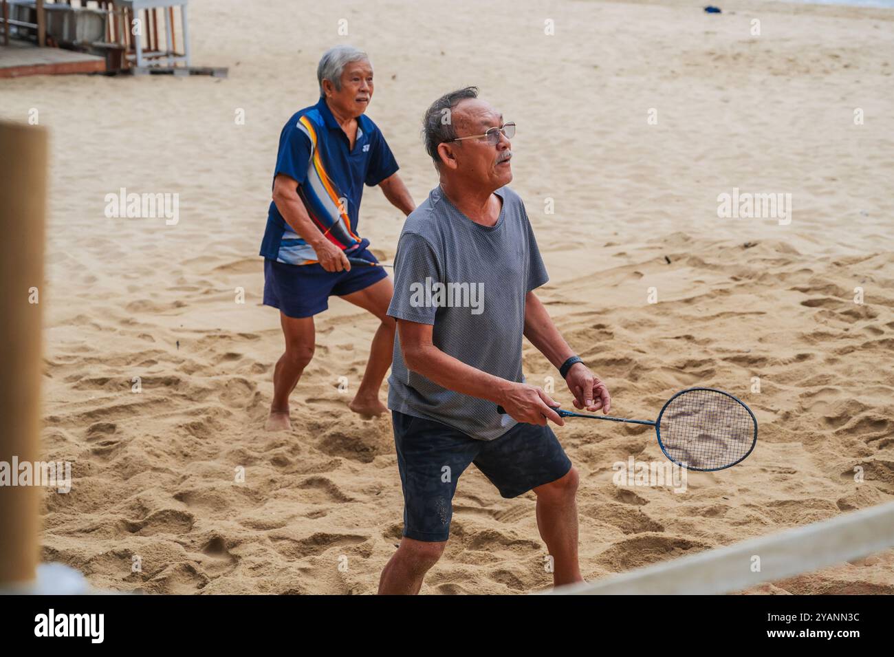 Elderly old Asian retired men play badminton with rackets on the beach ...