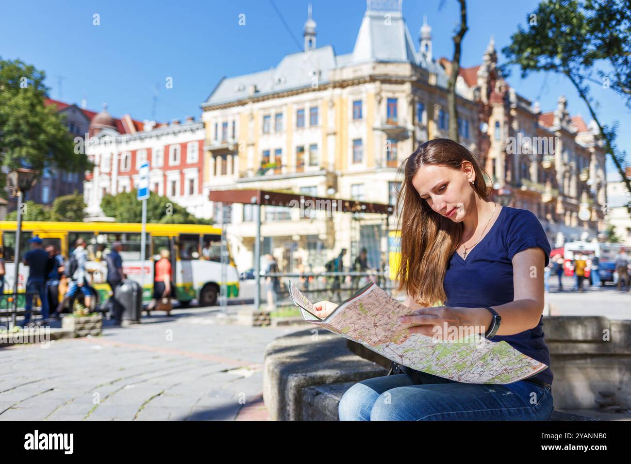 A woman sits outside, happily examining a map while enjoying the sunny ...