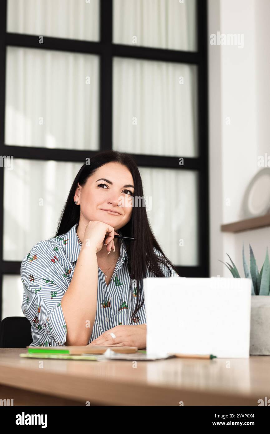 A young woman is thoughtfully pondering various ideas at her desk while ...