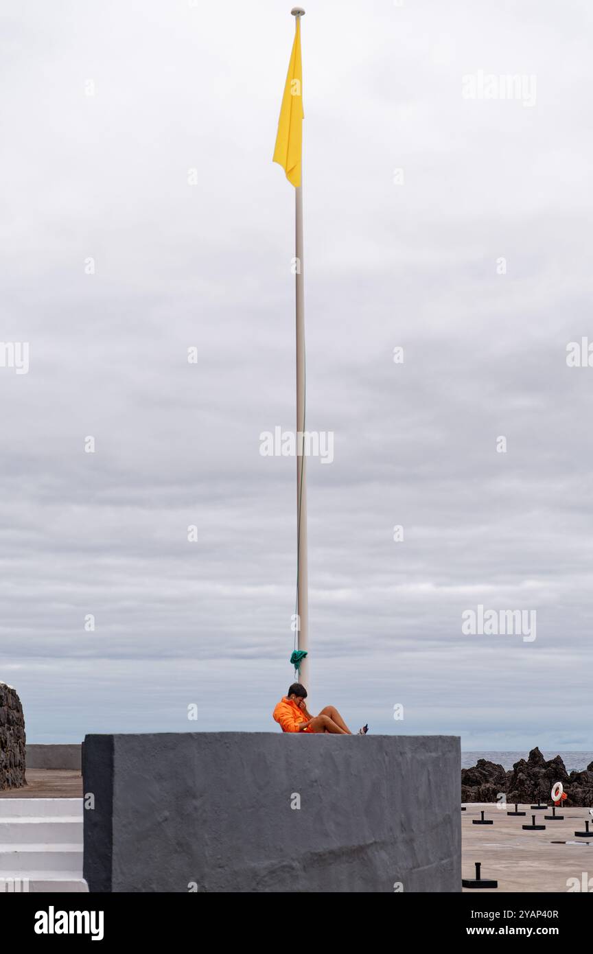 A lifeguard in bright orange relaxes beneath a yellow flag at Porto ...