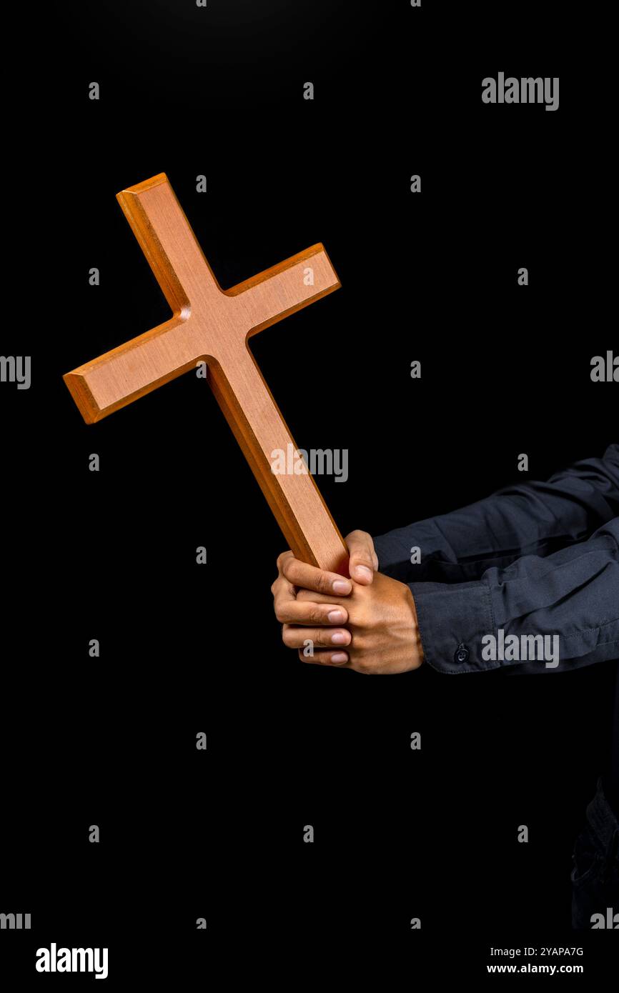 Man holding a wooden religion cross in his hand on black background ...