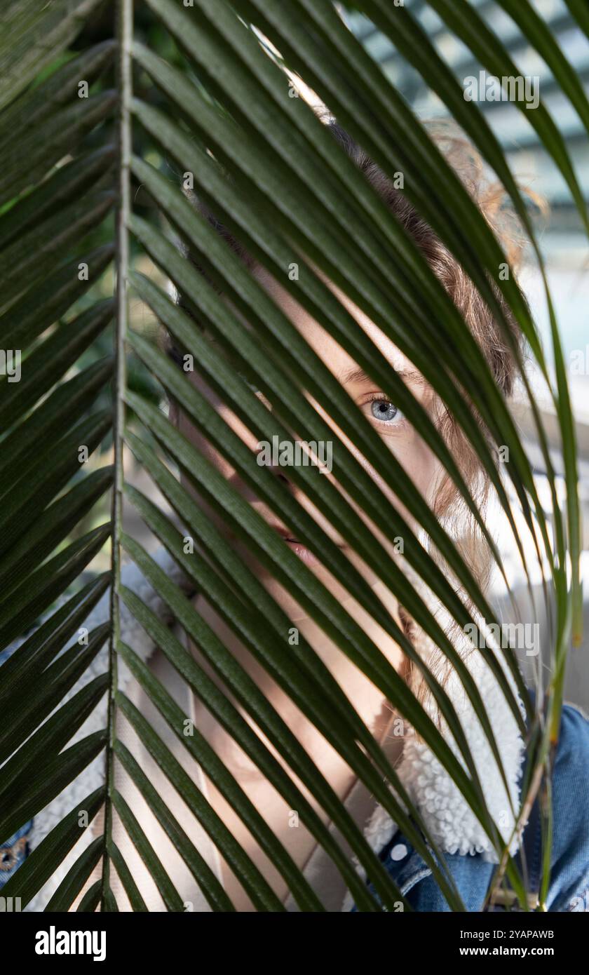 The face of a beautiful young girl, hidden behind large green palm ...