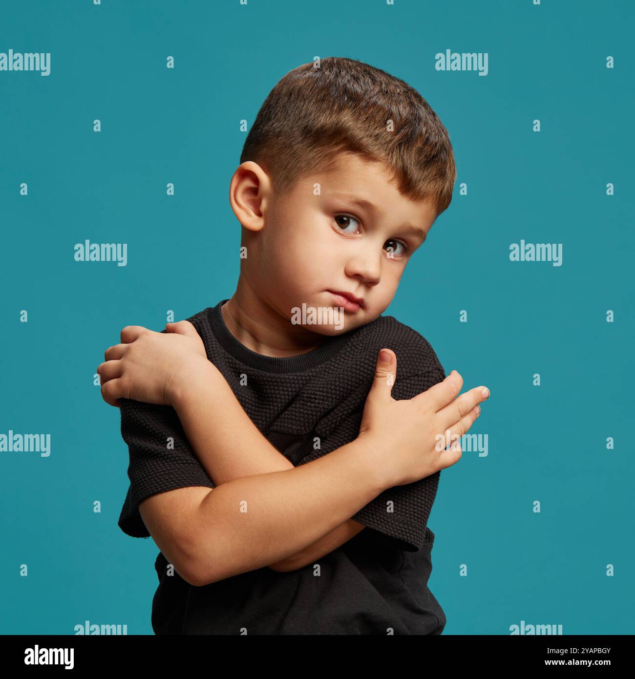 Preschool boy embraces himself with adorable expression blue studio ...