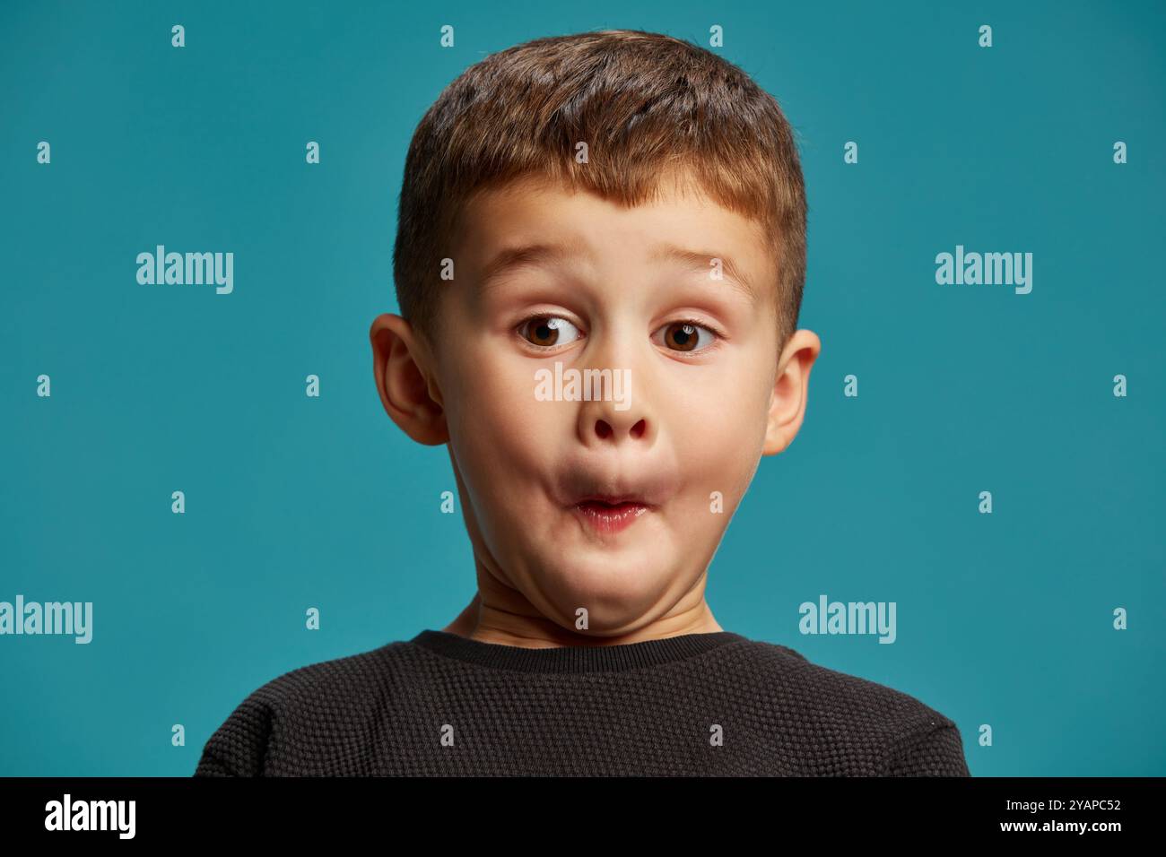 Boy makes comical expression with puffed cheeks, his eyes wide open in ...
