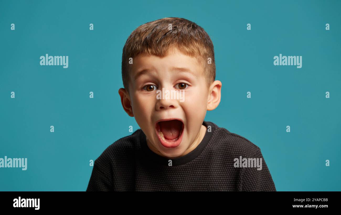 Boy appears to be in shock or surprise against blue studio background ...