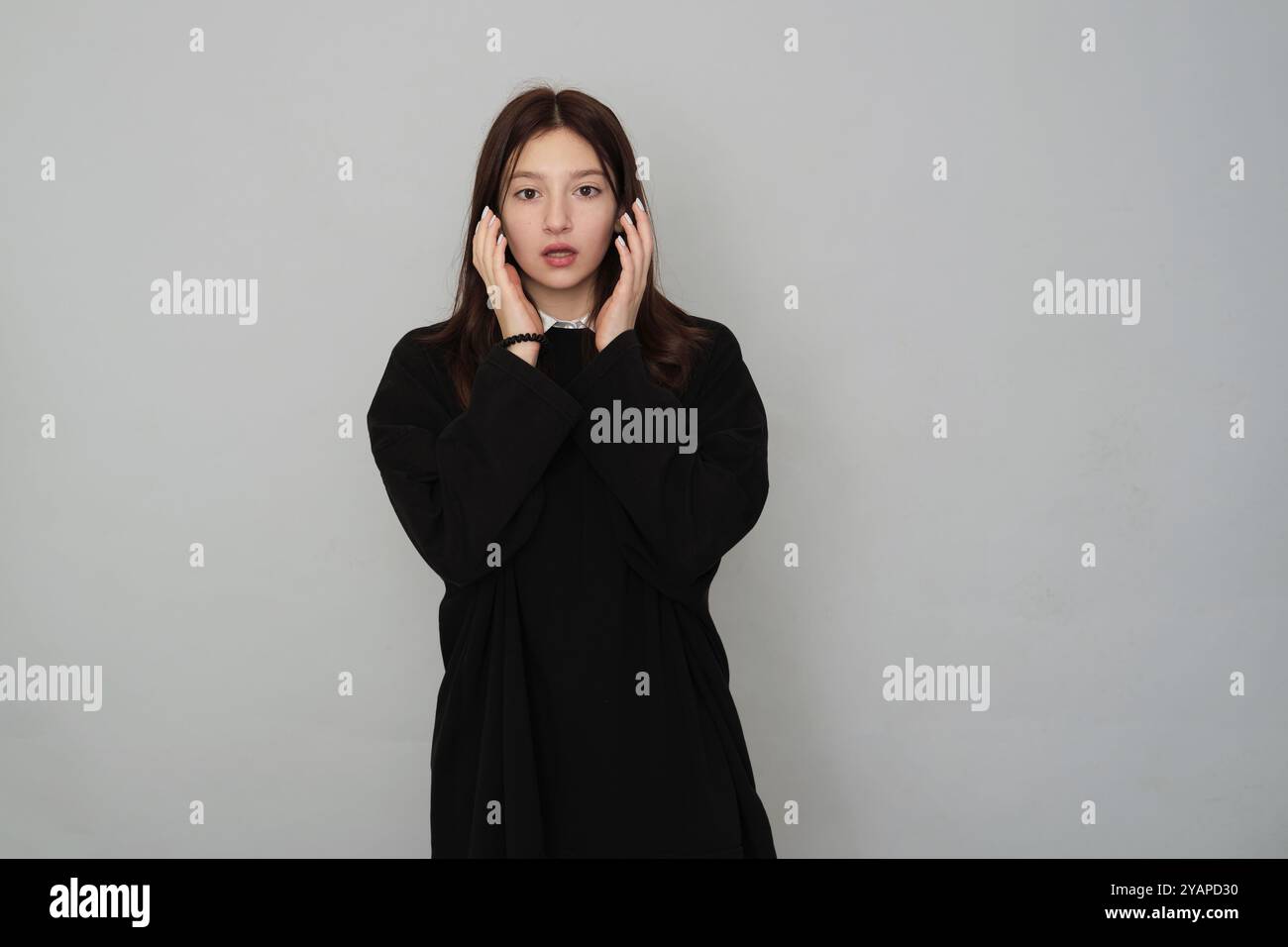 Shocked young woman holding her face, eyes wide with surprise. Conveys ...