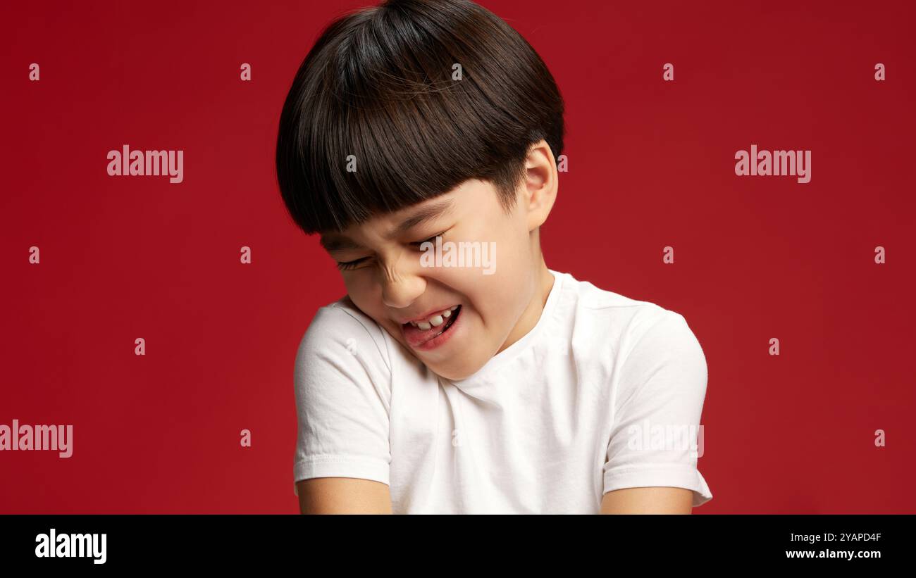 Little Asian boy bites his lip in a cheeky grin, his expression full of ...