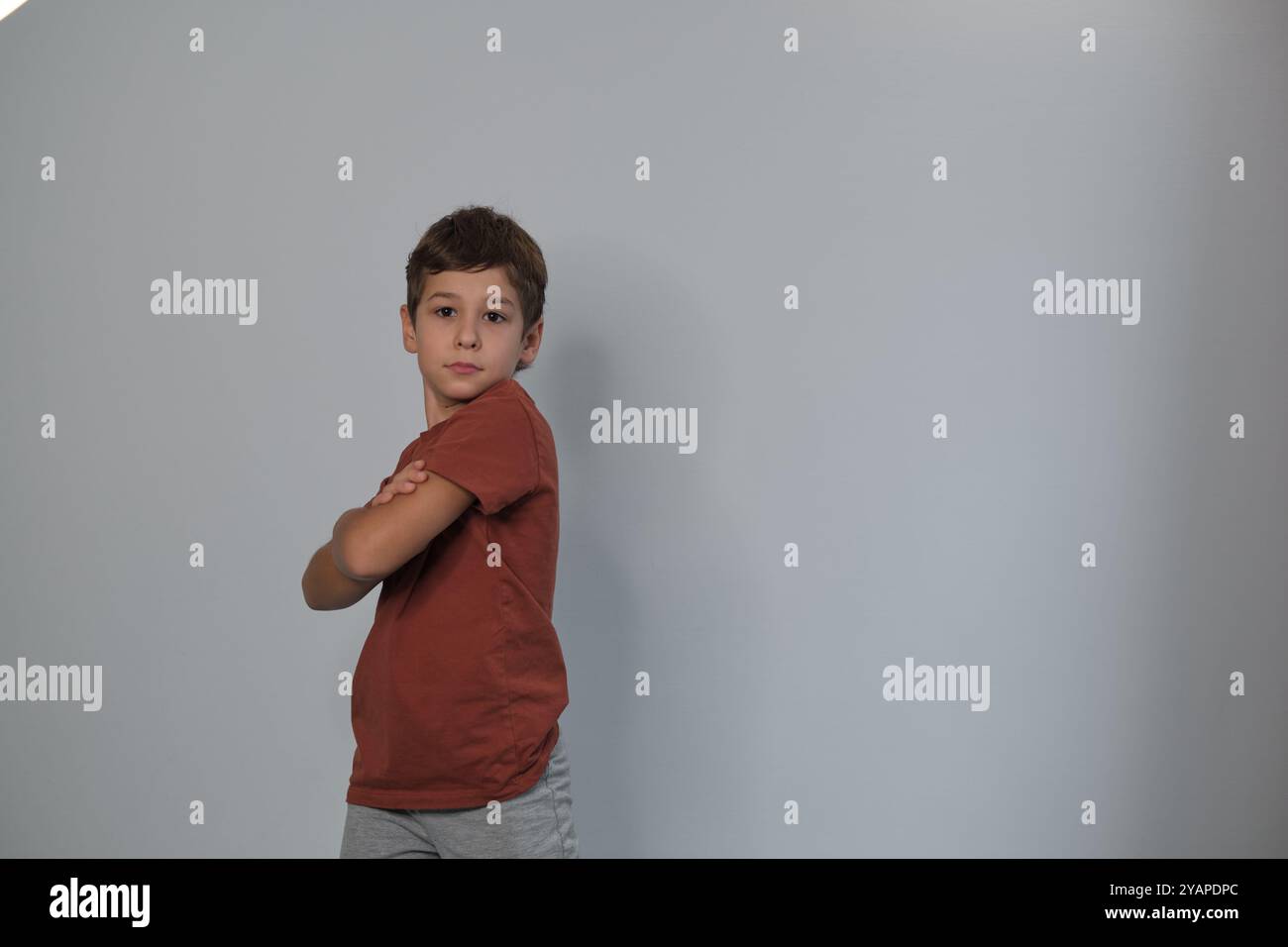 Arms crossed, a boy stands firm, showing determination. Reflects rising ...