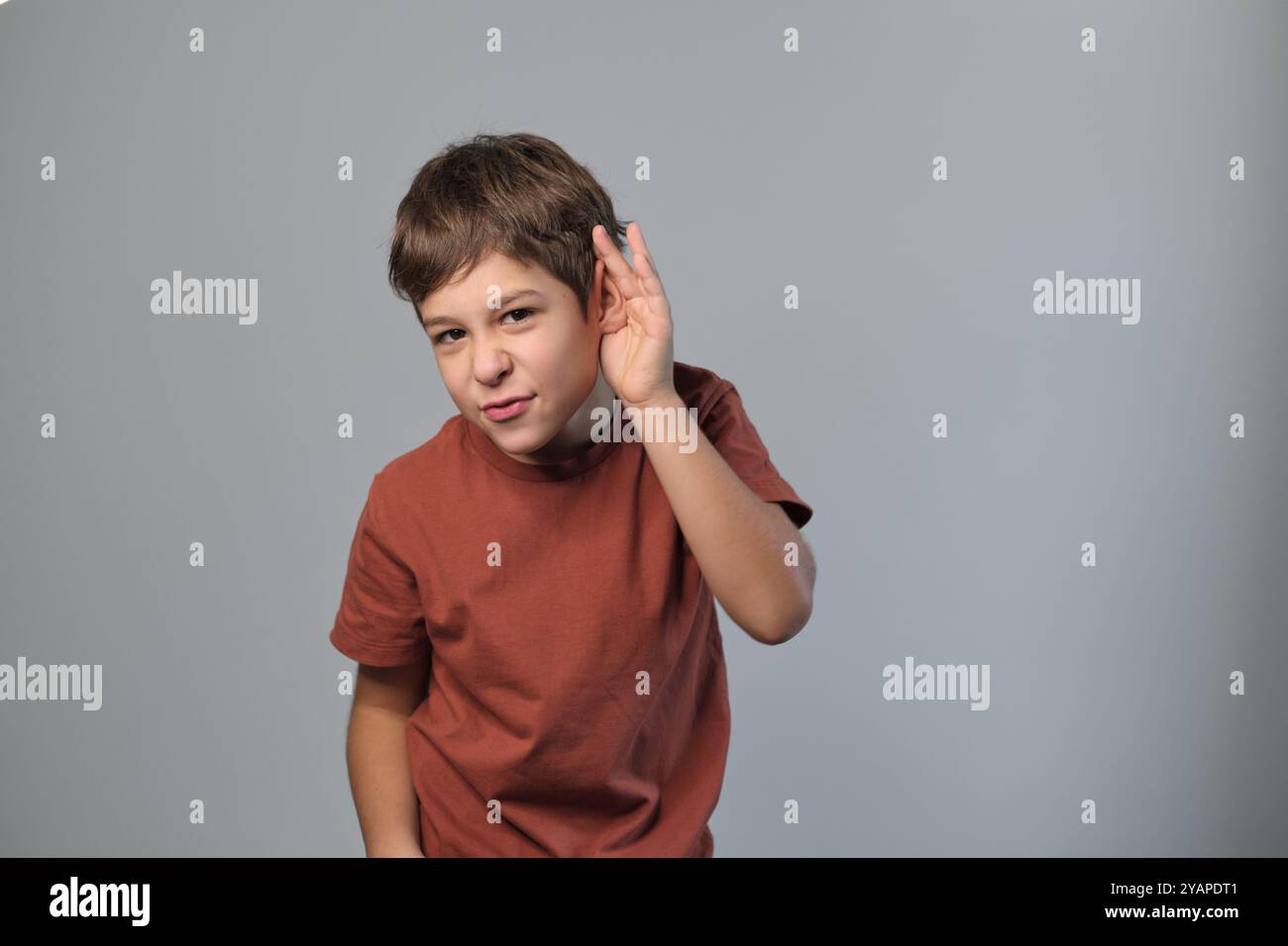 boy attentively listens, hand to ear, a gesture of focus. This image ...