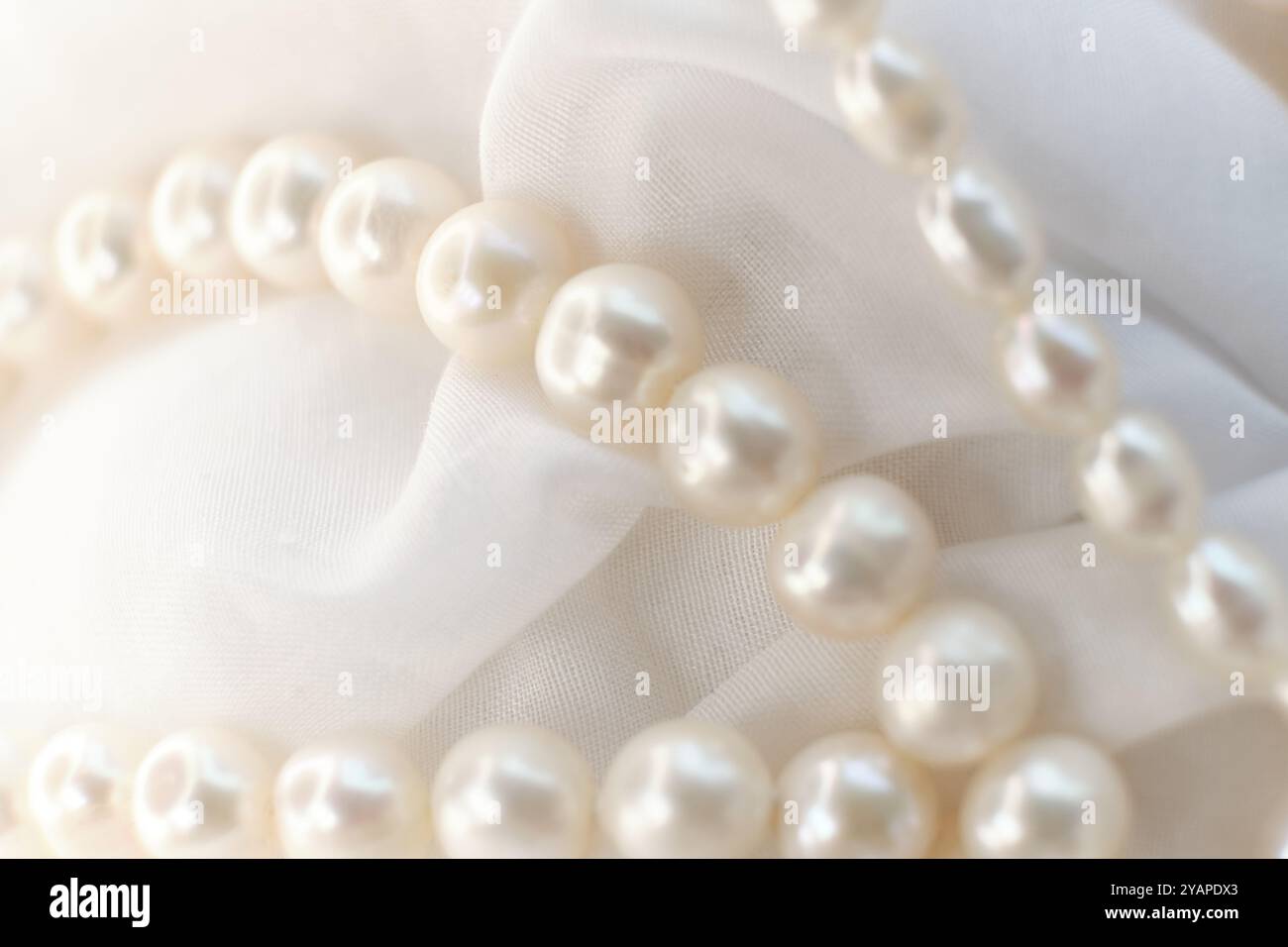 A string of natural pearls lay elegantly on a pale canvas, their soft ...