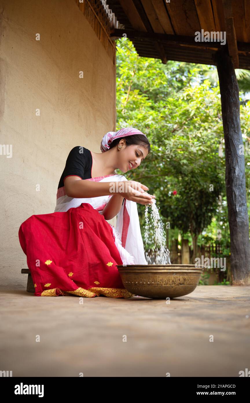 An Assamese girl diligently separates husk from rice using a ...