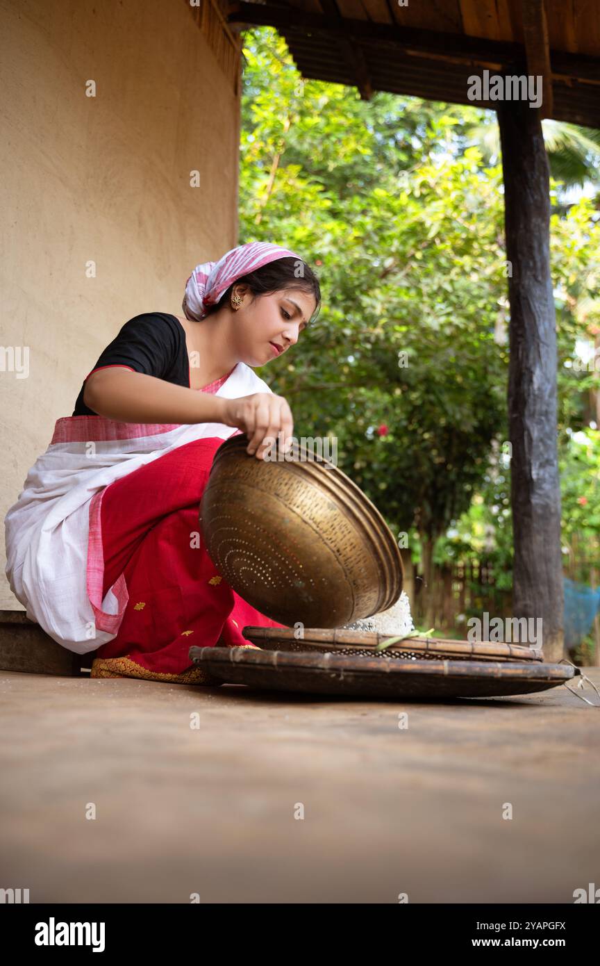 An Assamese girl diligently separates husk from rice using a ...