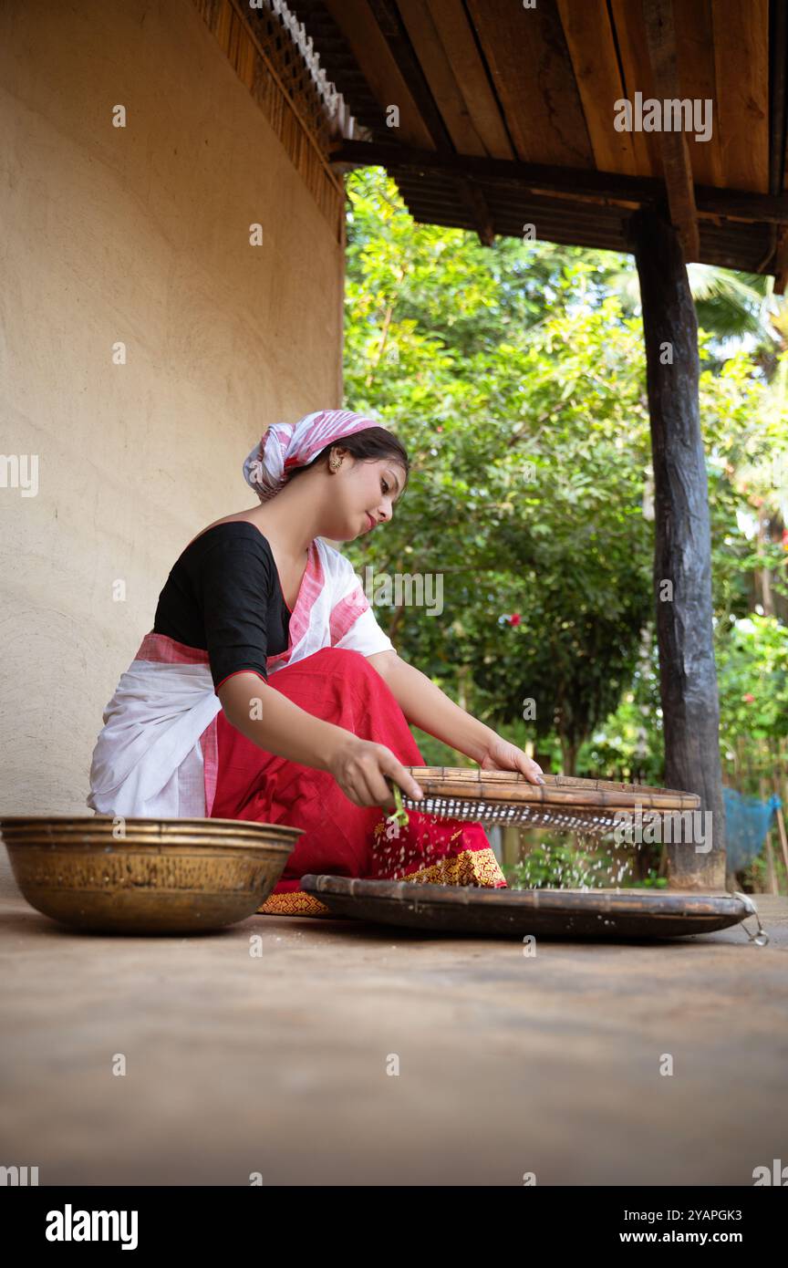An Assamese girl diligently separates husk from rice using a ...