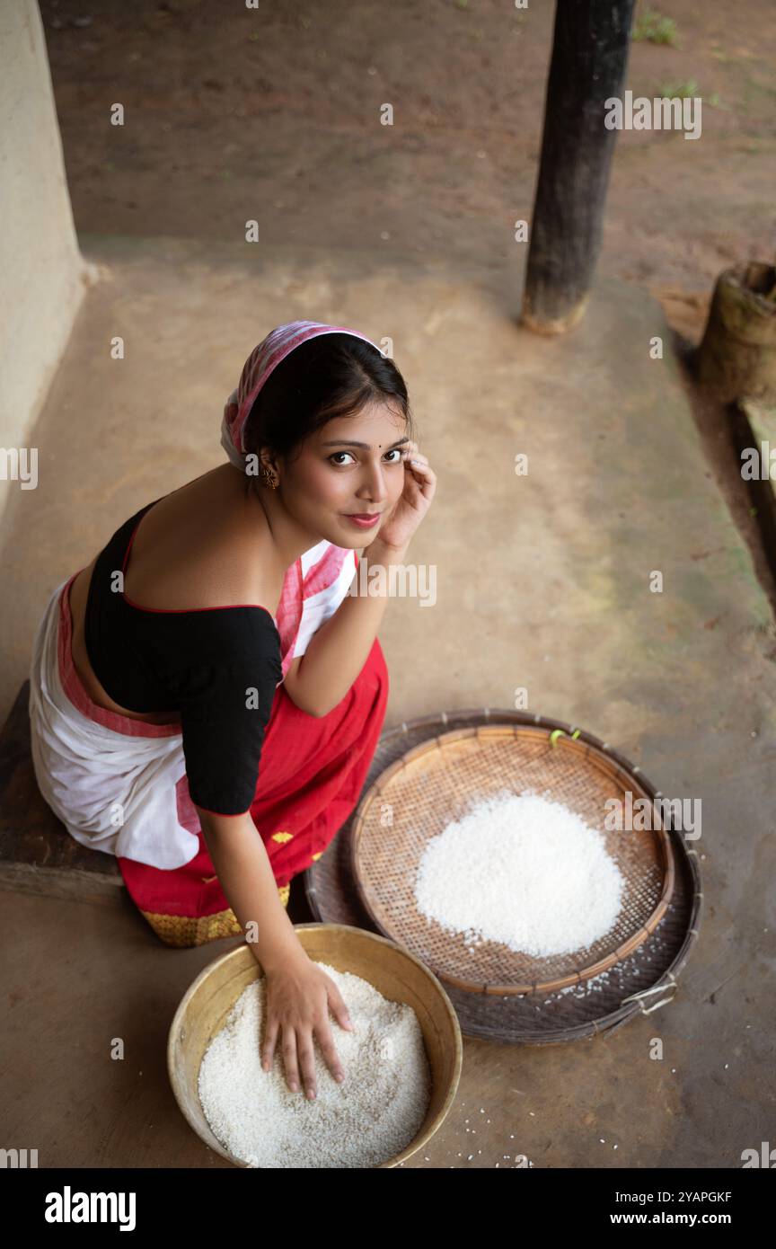 An Assamese girl diligently separates husk from rice using a ...