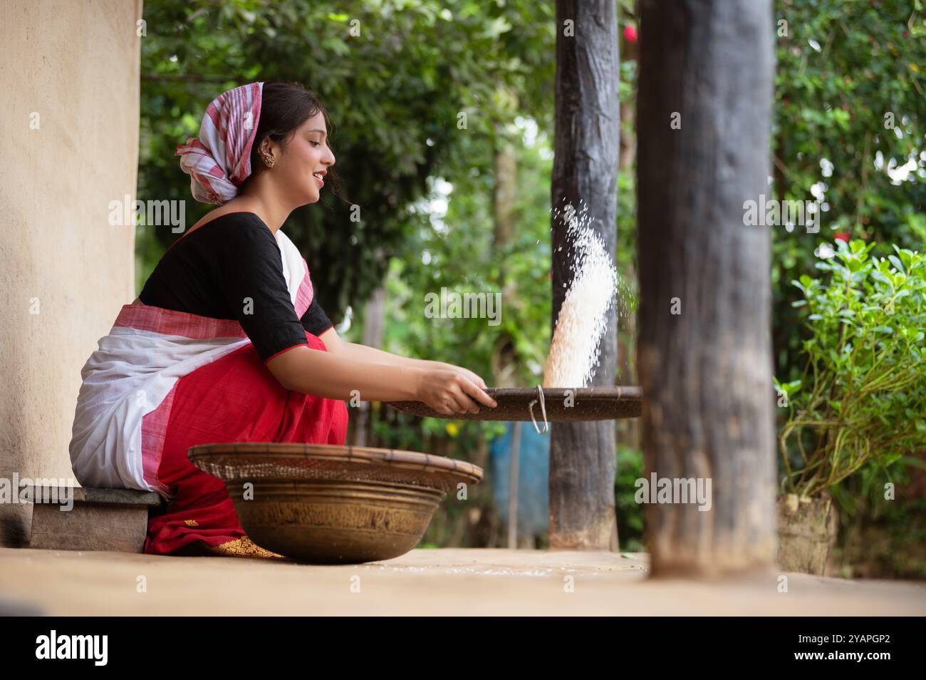 An Assamese girl diligently separates husk from rice using a ...