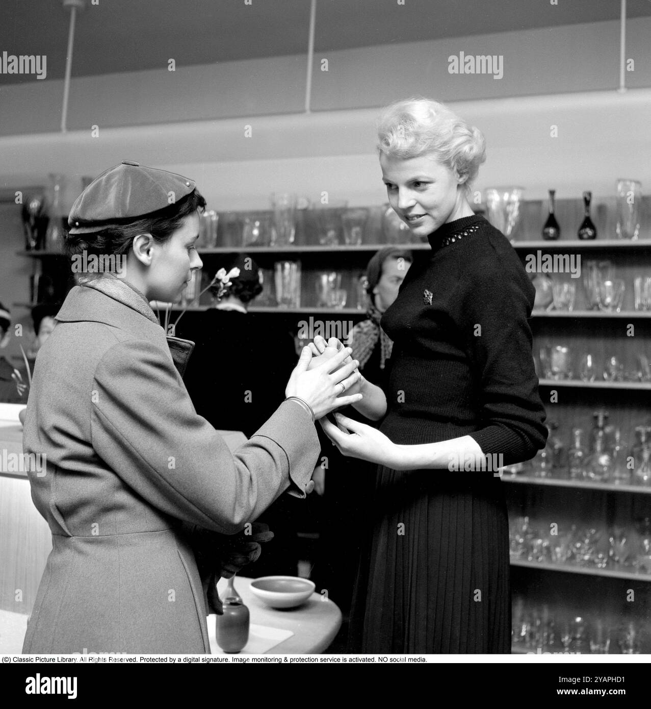 Shopping in the 1950s. A young woman in a store where a sales woman is ...