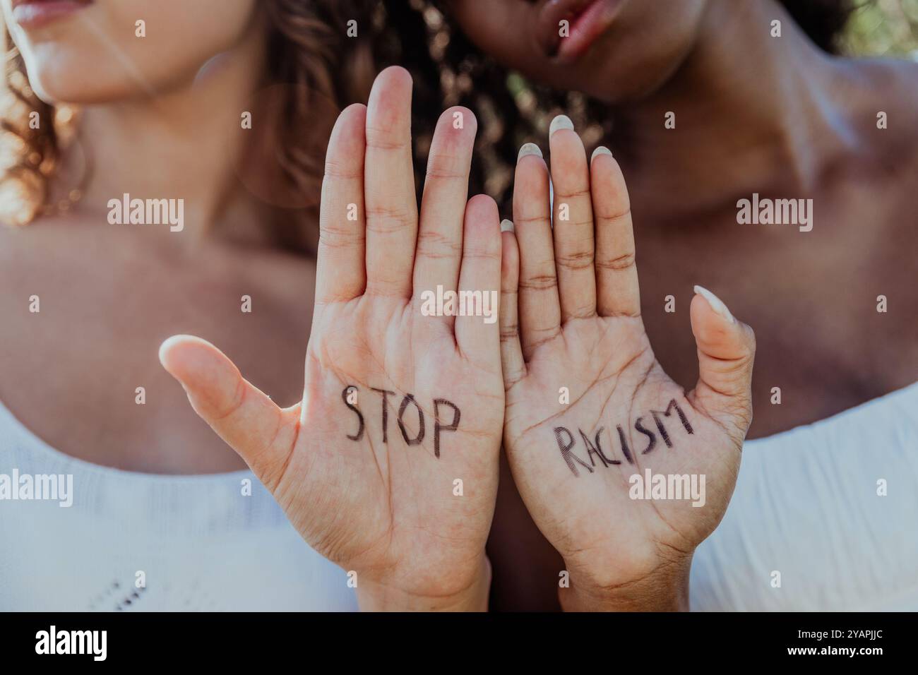 Two women are holding hands and writing "Stop Racism" on their hands ...