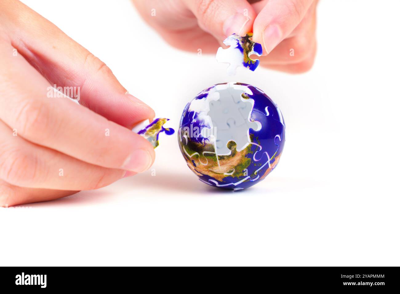 Two hands positioning a puzzle piece into a globe, highlighting the ...