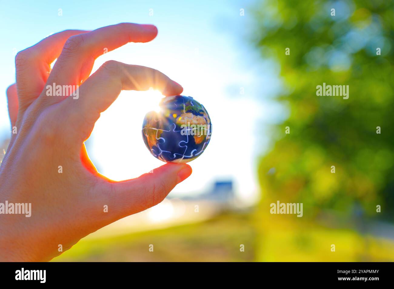 Hand holds a jigsaw puzzle globe, backlit by sunlight, showcasing a ...