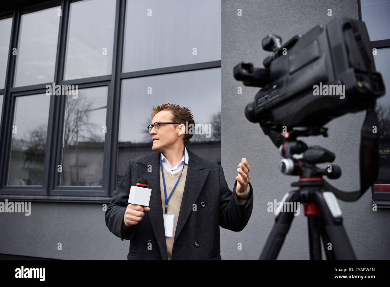 A journalist in glasses and coat actively reports with a microphone in ...