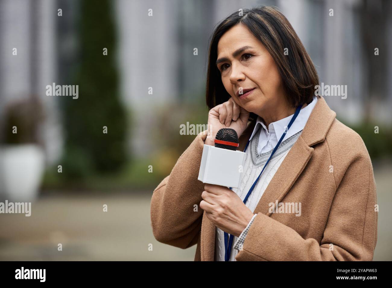 A multiracial female journalist in a beige coat is holding a microphone ...