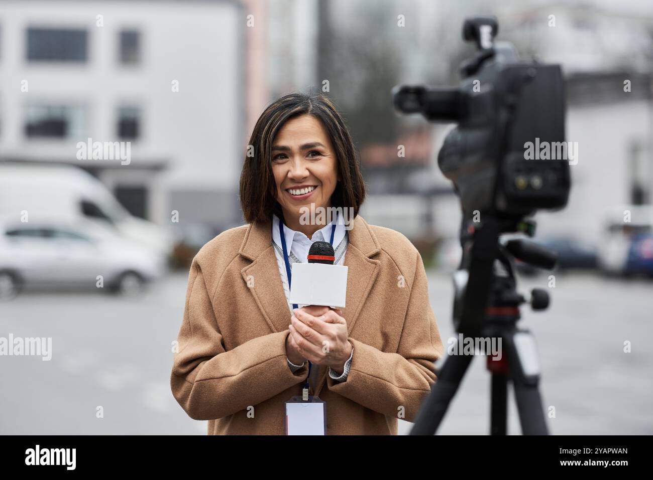A multiracial female journalist in a beige coat reports live outdoors ...
