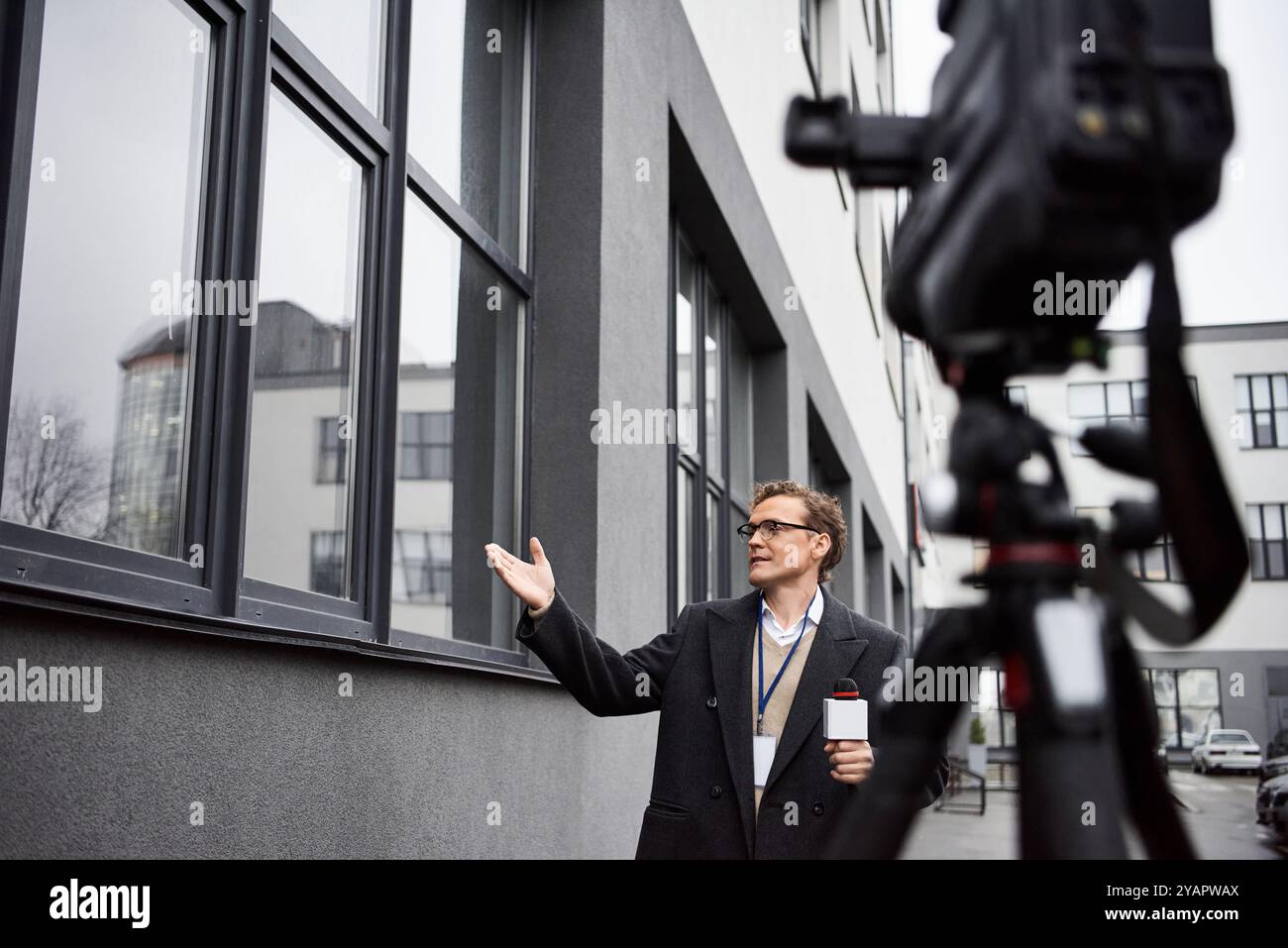 A news anchor in glasses and a coat engages with an audience, holding a ...