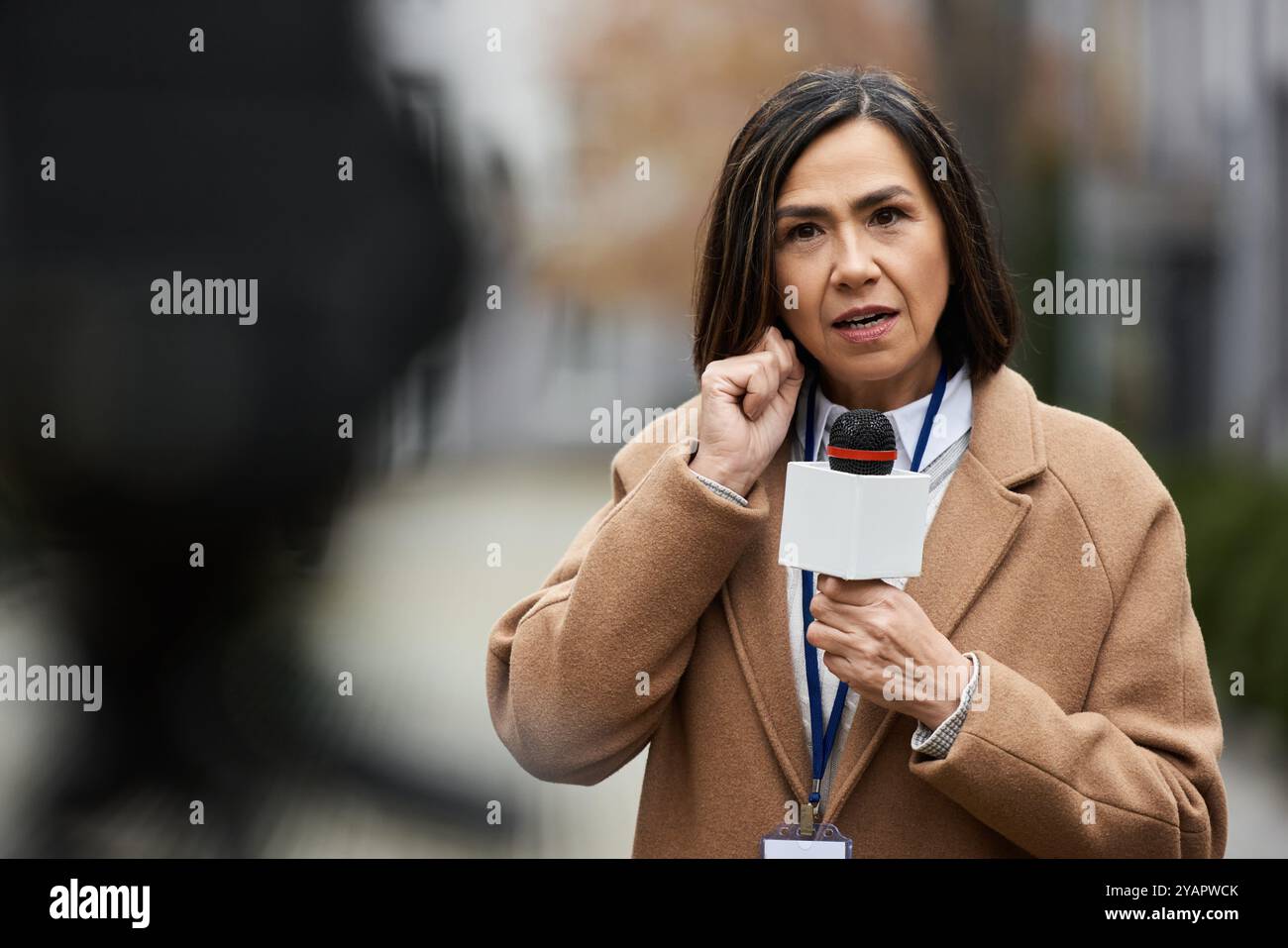 A skilled journalist in a beige coat speaks into her microphone ...