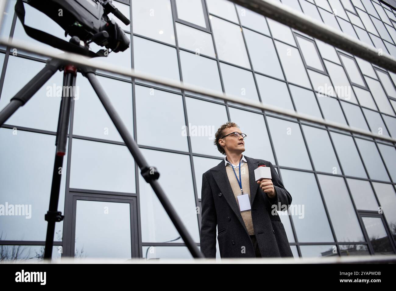 A professional journalist in glasses stands with a microphone ...
