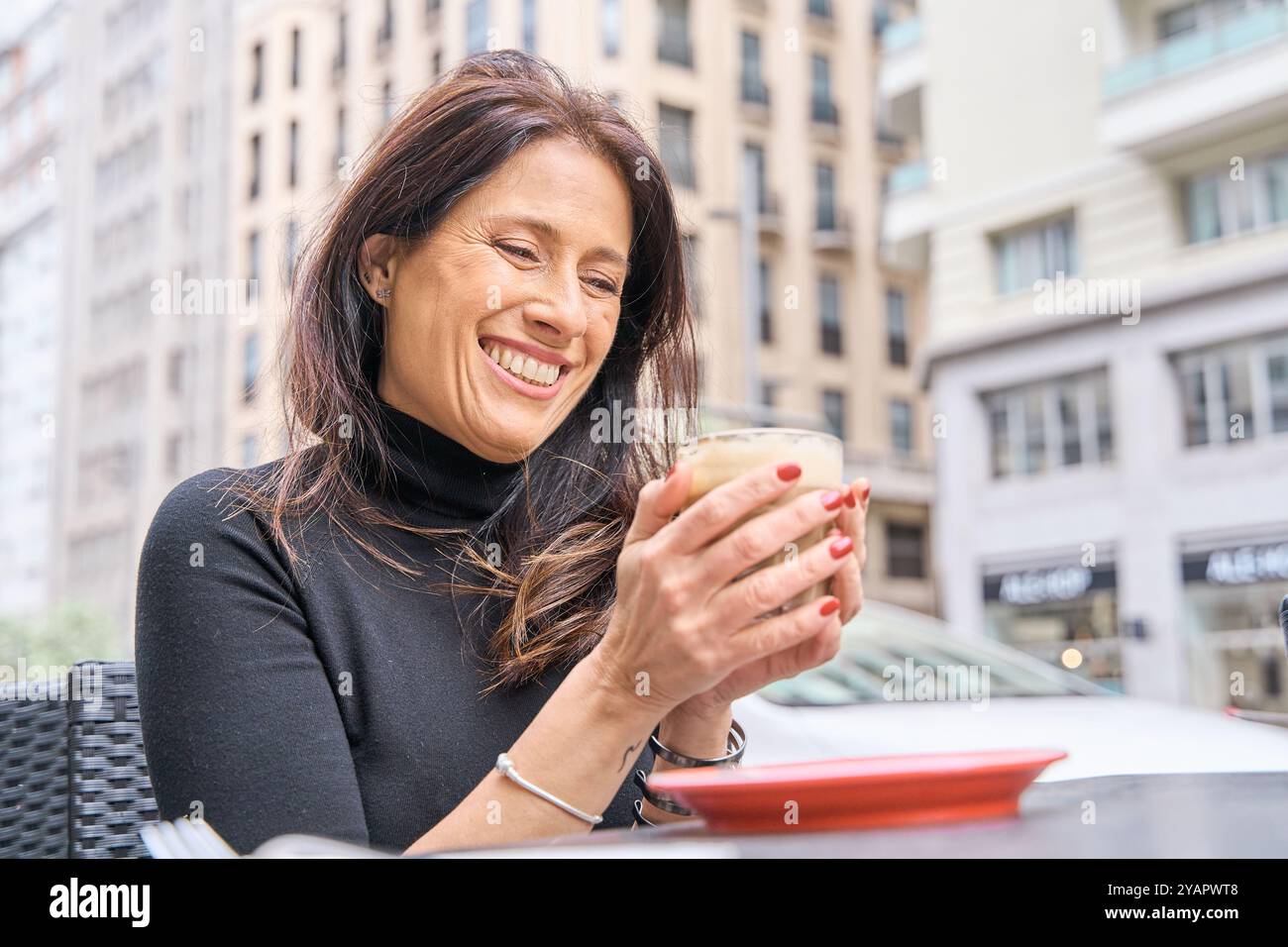 middle-aged woman sitting on the terrace of a bar with a coffee in hand ...