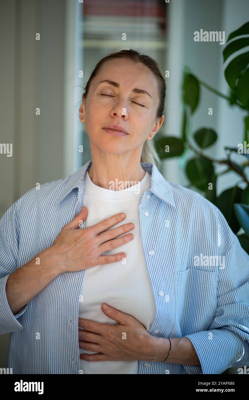 Peaceful calm woman holding hands on chest with closed eyes feels ...