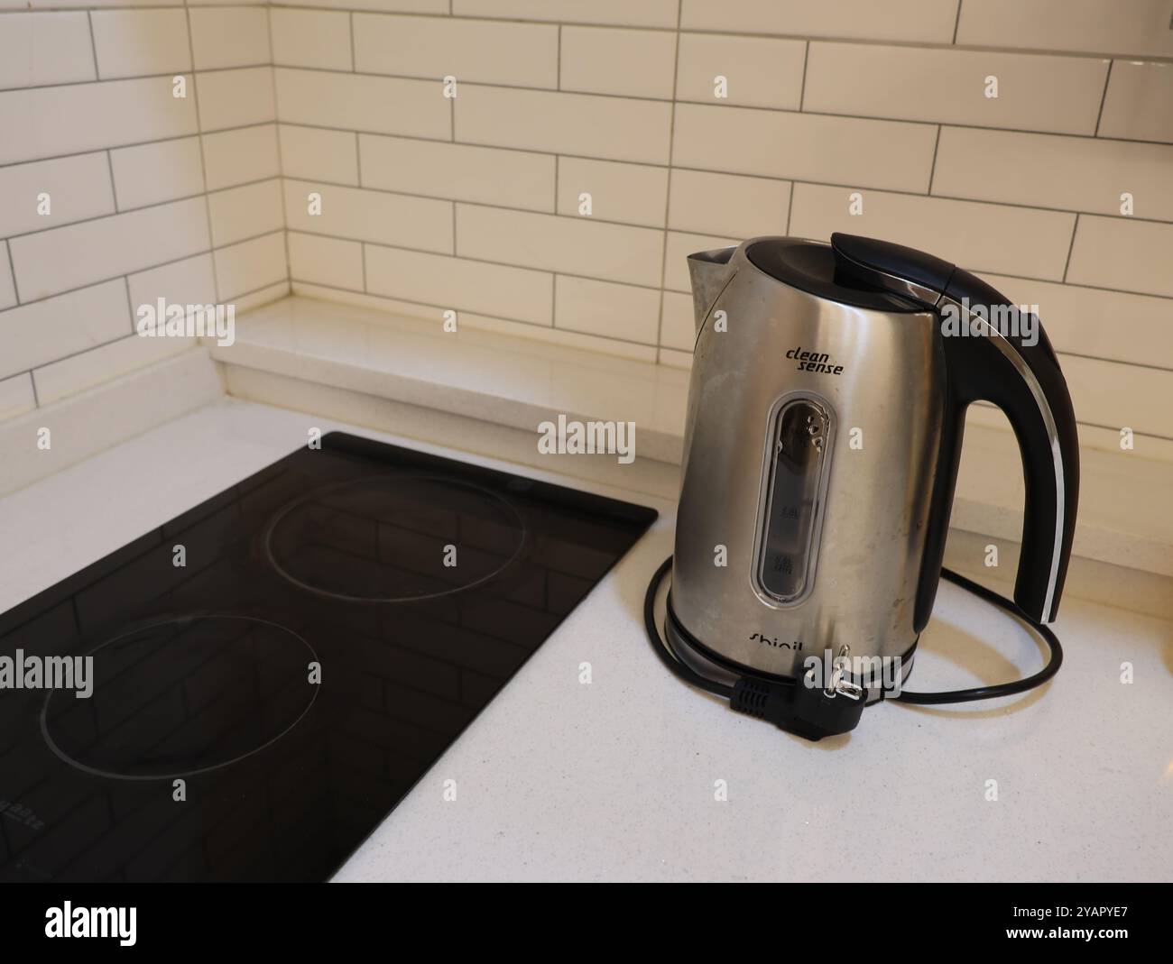 A silver tea kettle sits on a white counter next to a black stove. The ...