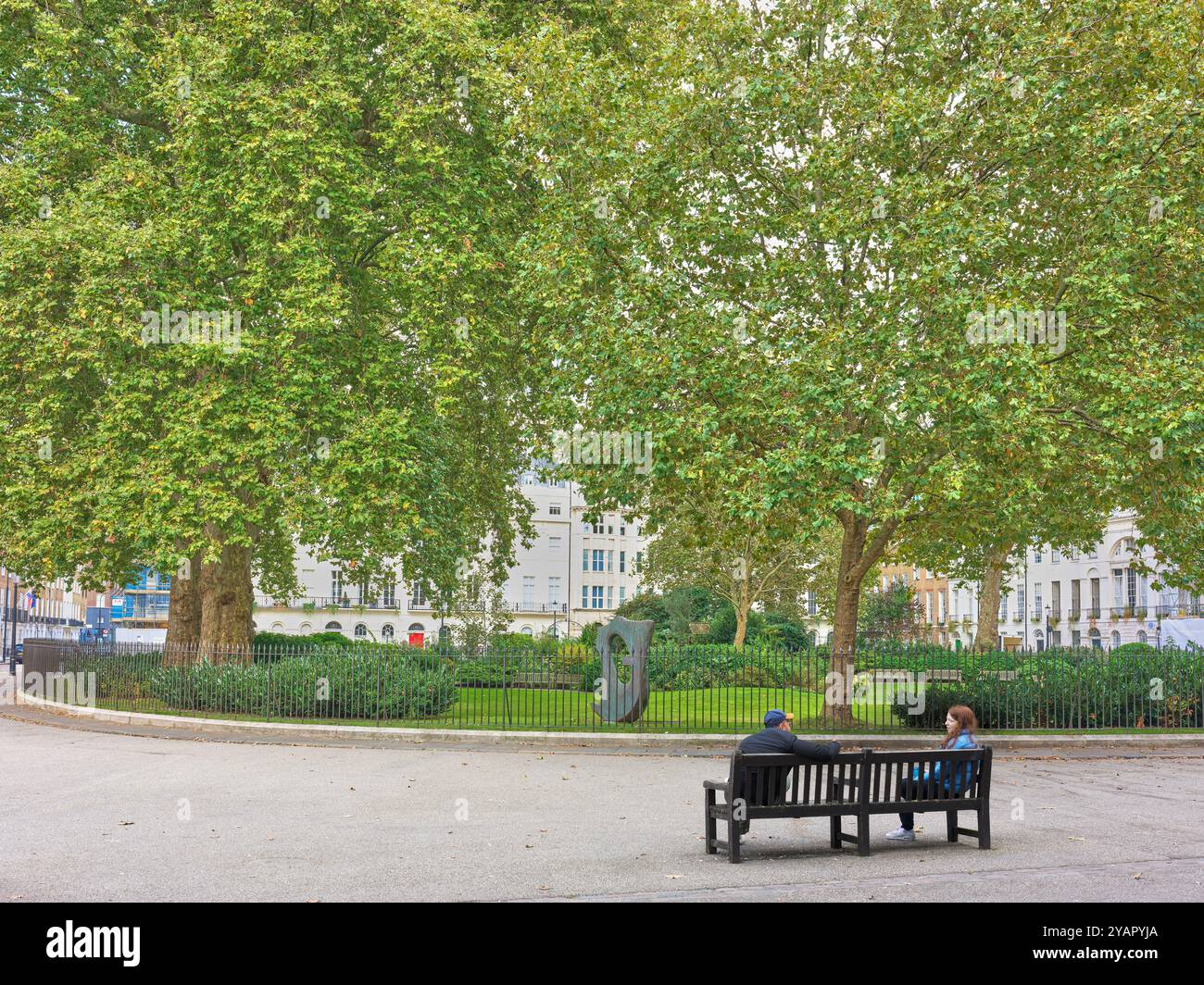 A couple sit on a bench outside the garden at Fitzroy Square, London ...