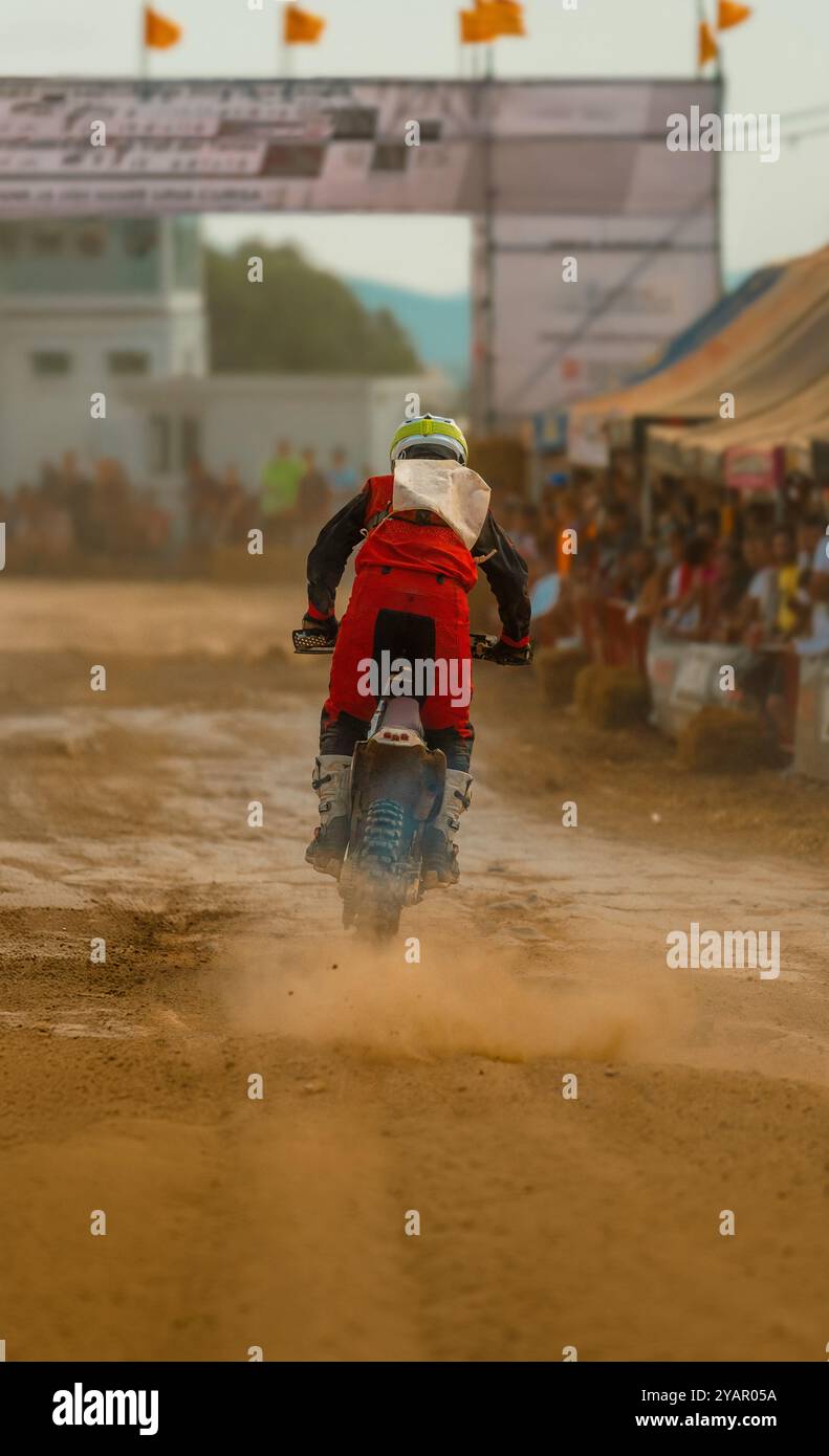 Motocross rider standing on his footpegs in action racing down a dirt road creating a lot of ...