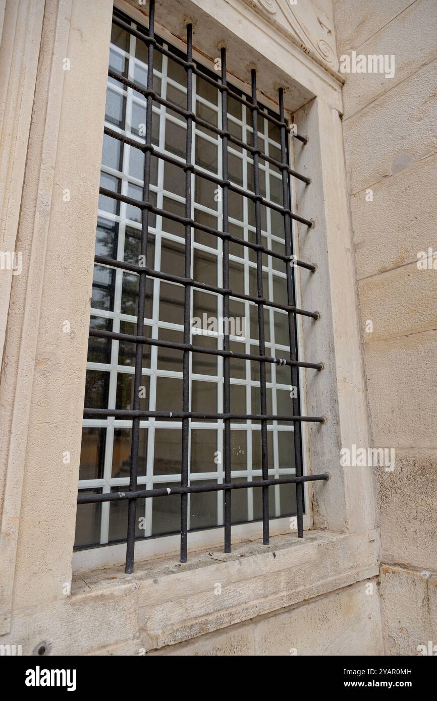 A classic stone-framed window with metal bars and a grid-patterned ...
