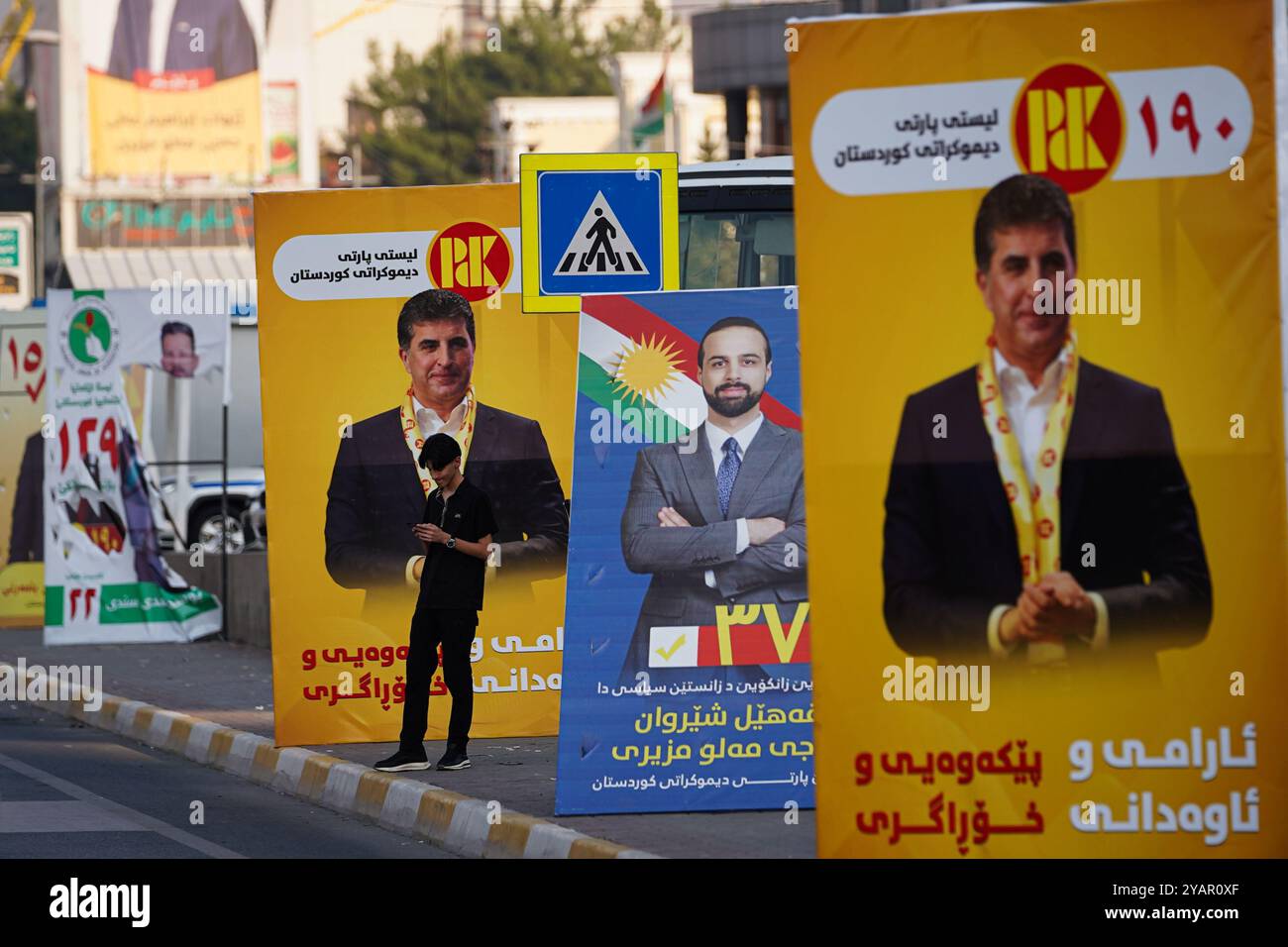 Duhok, Iraq. 13th Oct, 2024. A young man stands alongside electoral ...