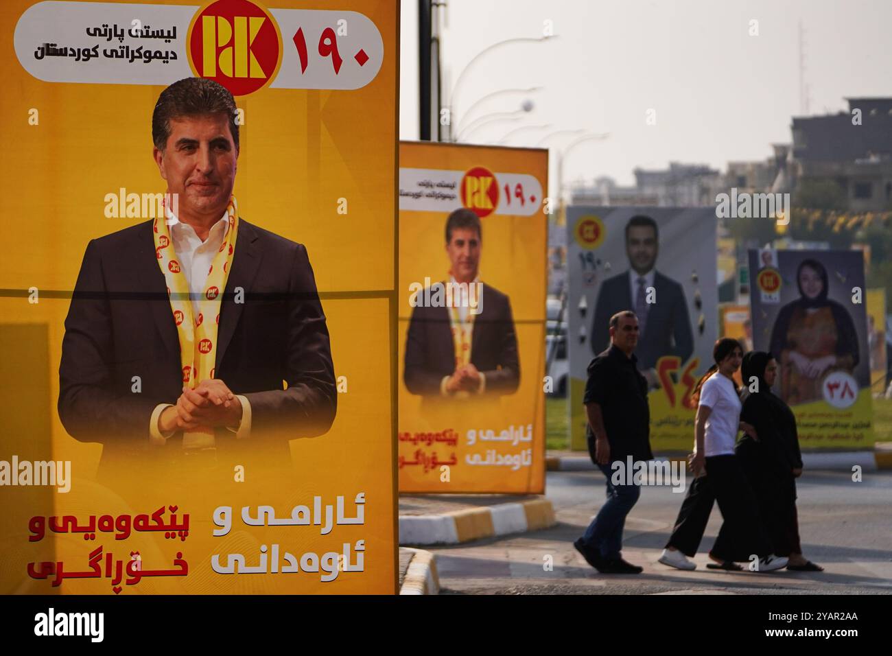 Duhok, Iraq. 13th Oct, 2024. People walk past electoral banners of the ...