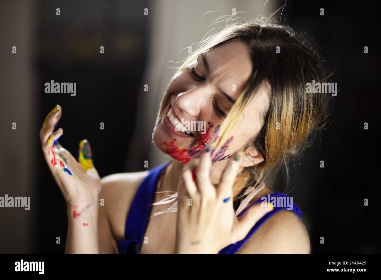 A joyful woman artist coated in colorful paint gestures happily in her ...