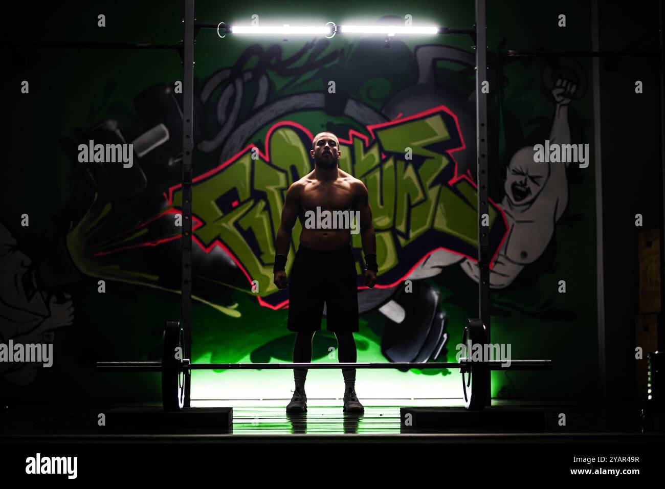 A strong, muscular man stands ready in front of a weightlifting bar in ...