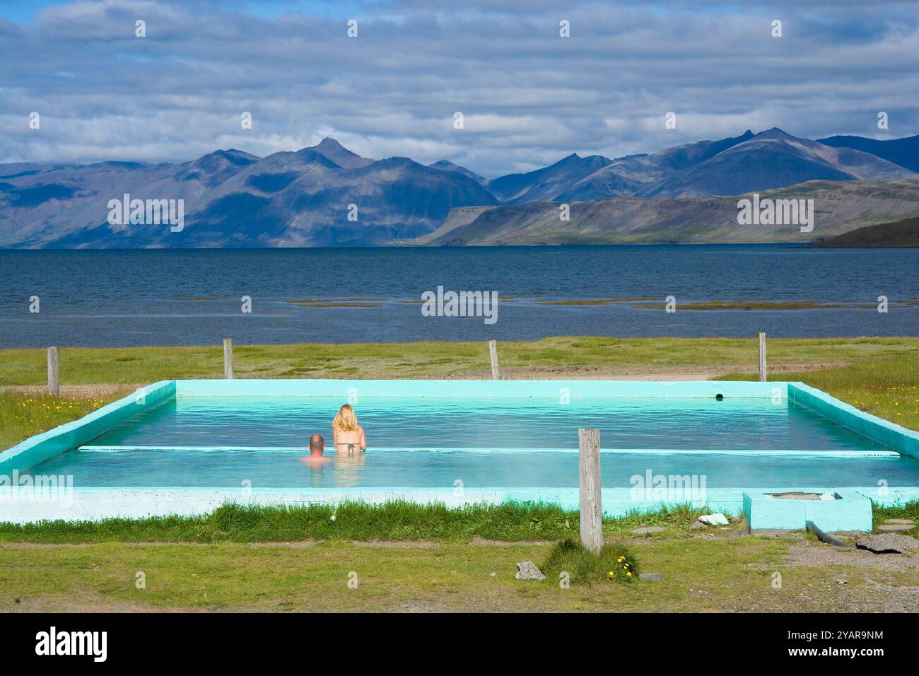 Outdoor geothermal pool against the backdrop of mountains and water in ...