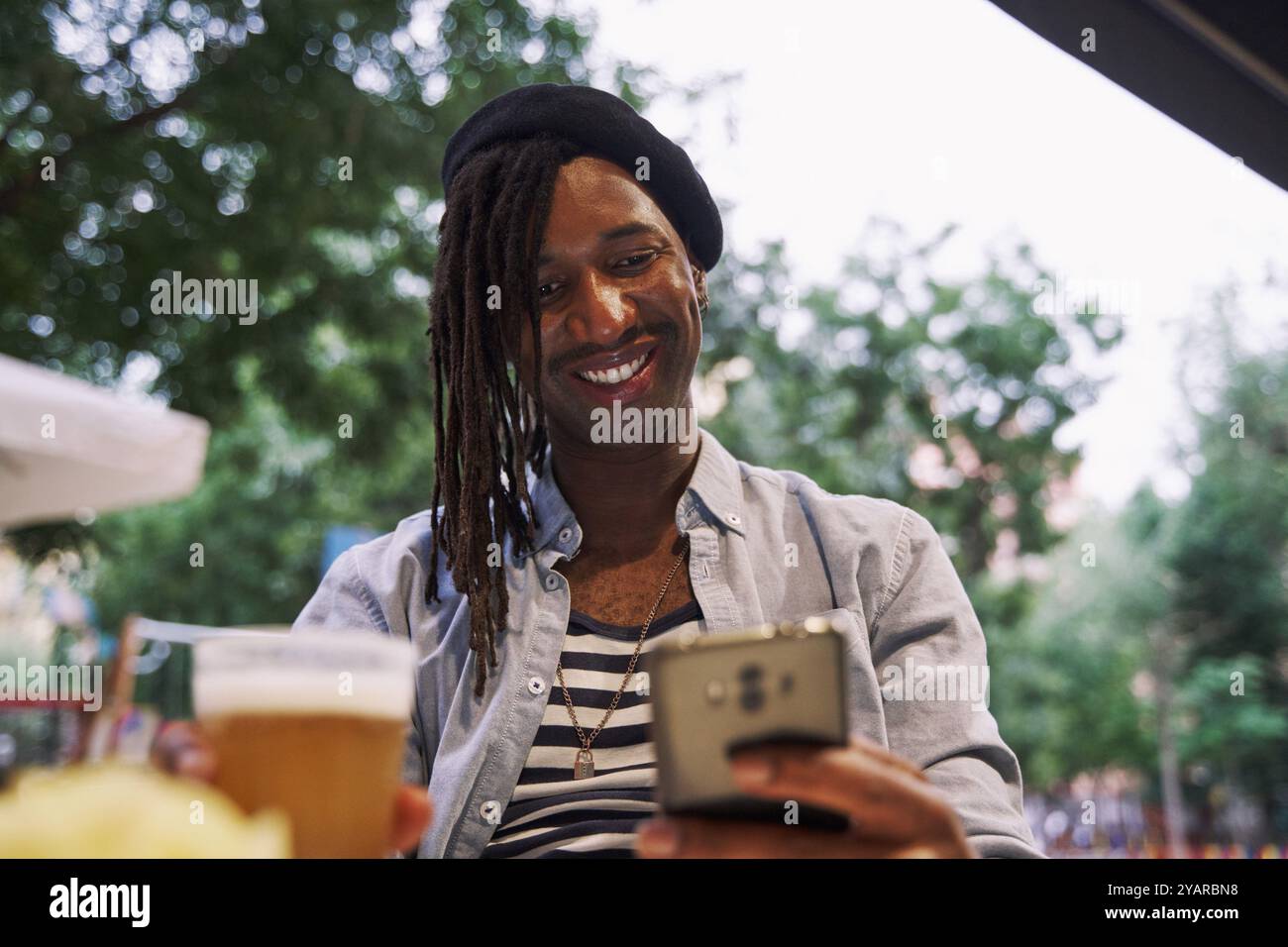 black man sitting in a bar drinking beer with his smartphone Stock ...