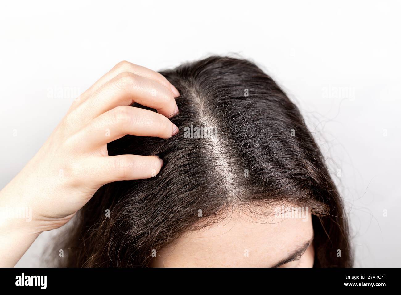 The woman scratches her head with her hand, showing a parting of dark ...